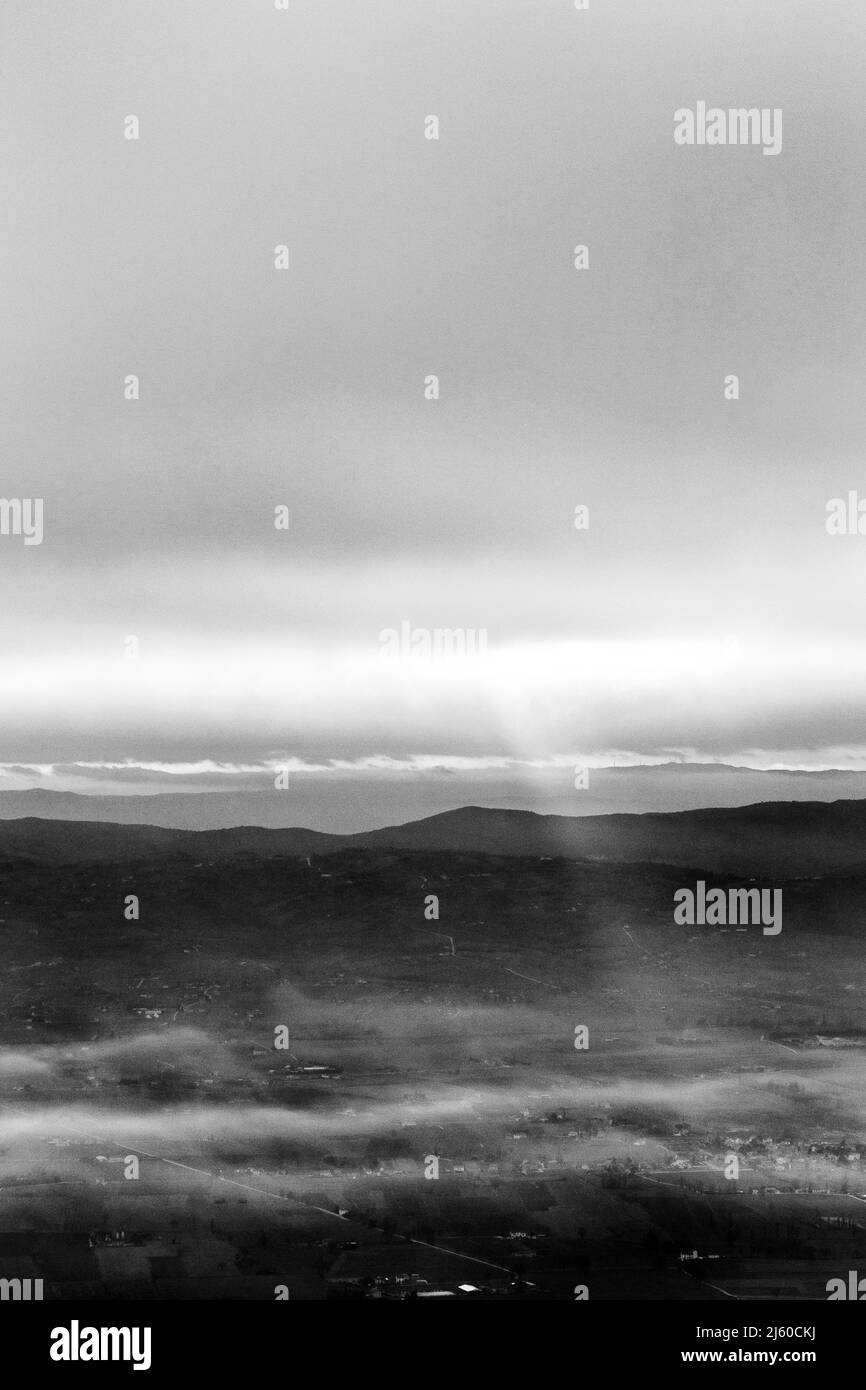 Sun rays coming down from some clouds over a valley filled by fog ...