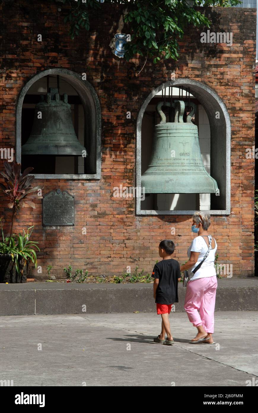 Grandmother and boy walking past large bells, San Sebastian Cathedral ...
