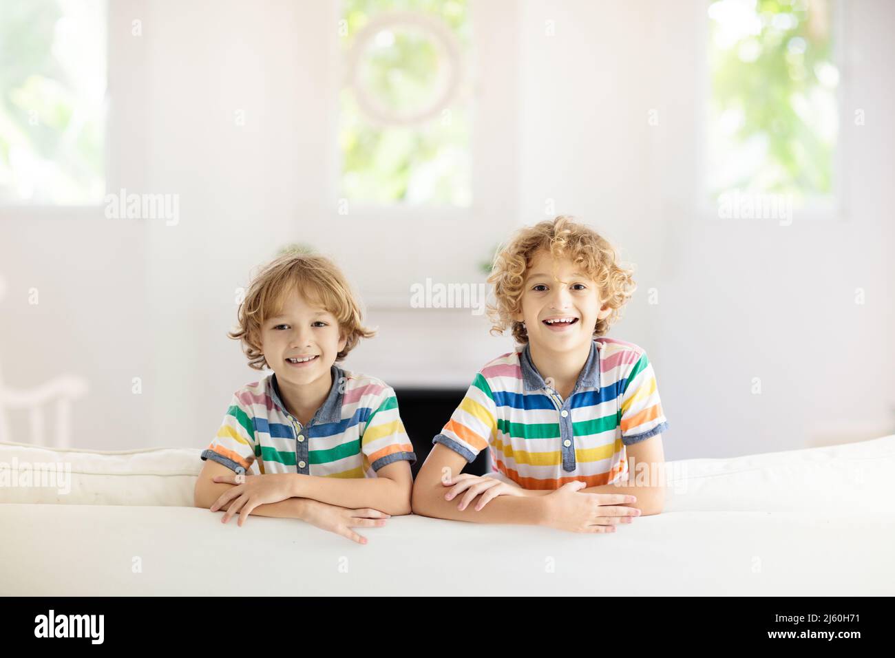 Kids play and watch tv on white couch. Children at home. Sunny family ...