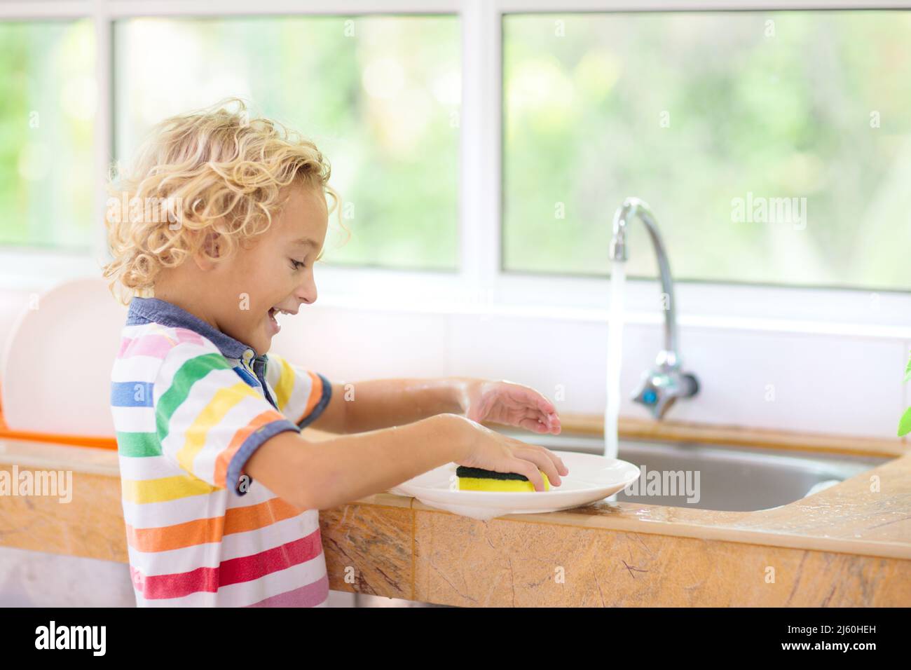 Child washing dishes. Home chores. Kid in white kitchen cleaning plates ...