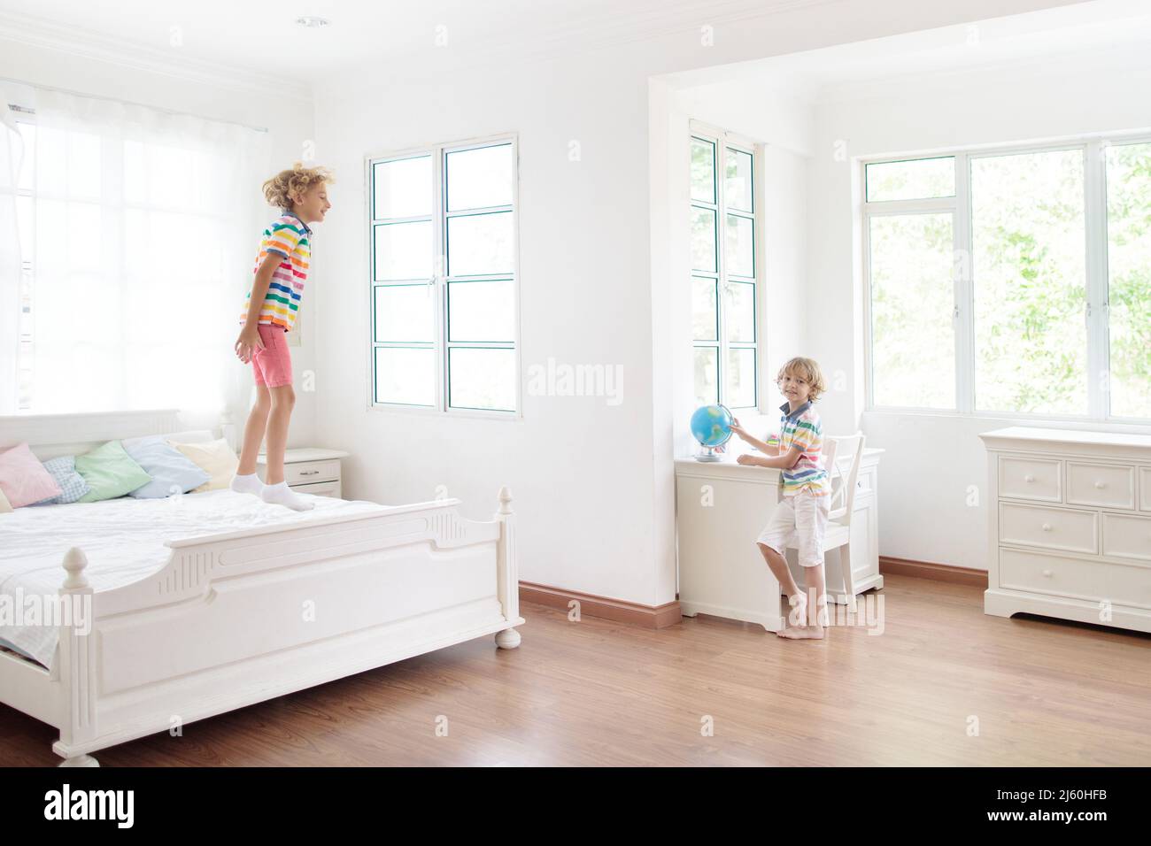 Child jumping on bed in white bedroom with big window. Kids play at ...