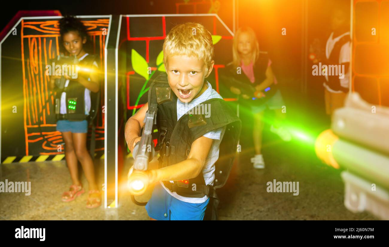 Emotional teen boy with laser pistol playing laser tag with friends on ...