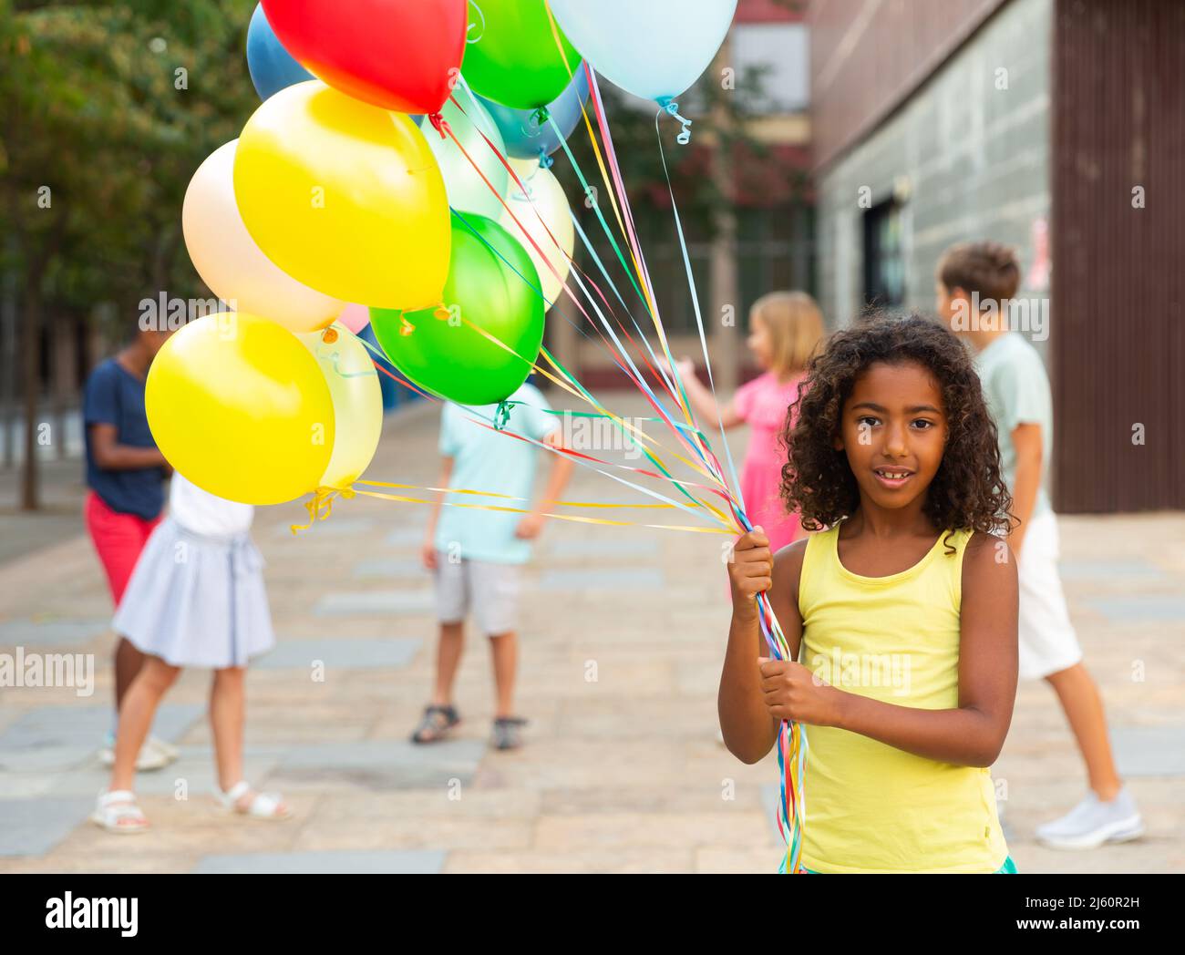 Smiling african american tween girl with balloons on city street Stock ...