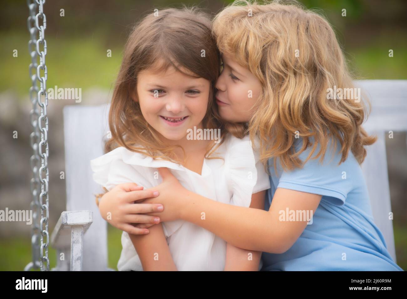 Two little children hug and kiss each other in summer garden. Kids ...