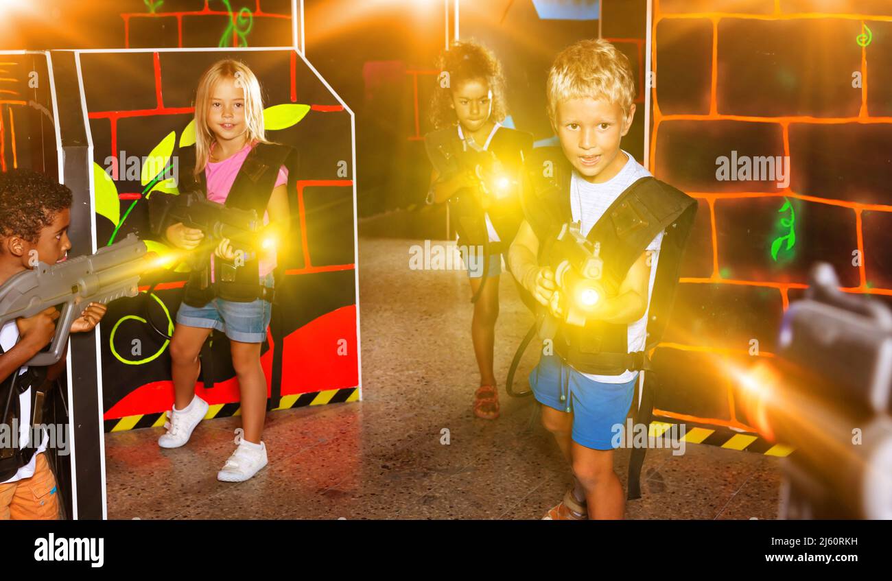 Modern teenage girl and boys with laser guns playing laser tag on dark ...