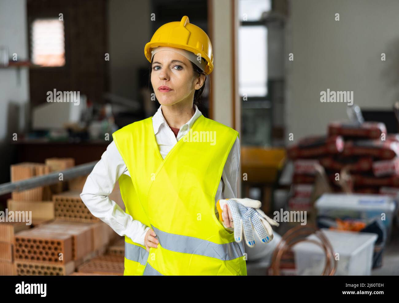 Portrait of woman builder in yellow vest and hardhat filling documentation during repair works ...