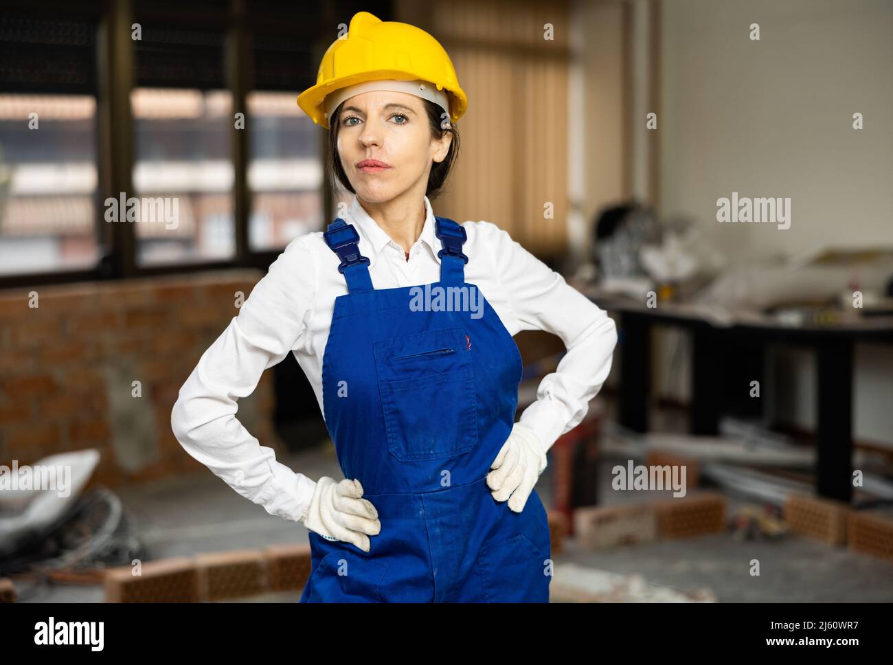 Confident female foreman in blue overalls and hard hat standing at ...