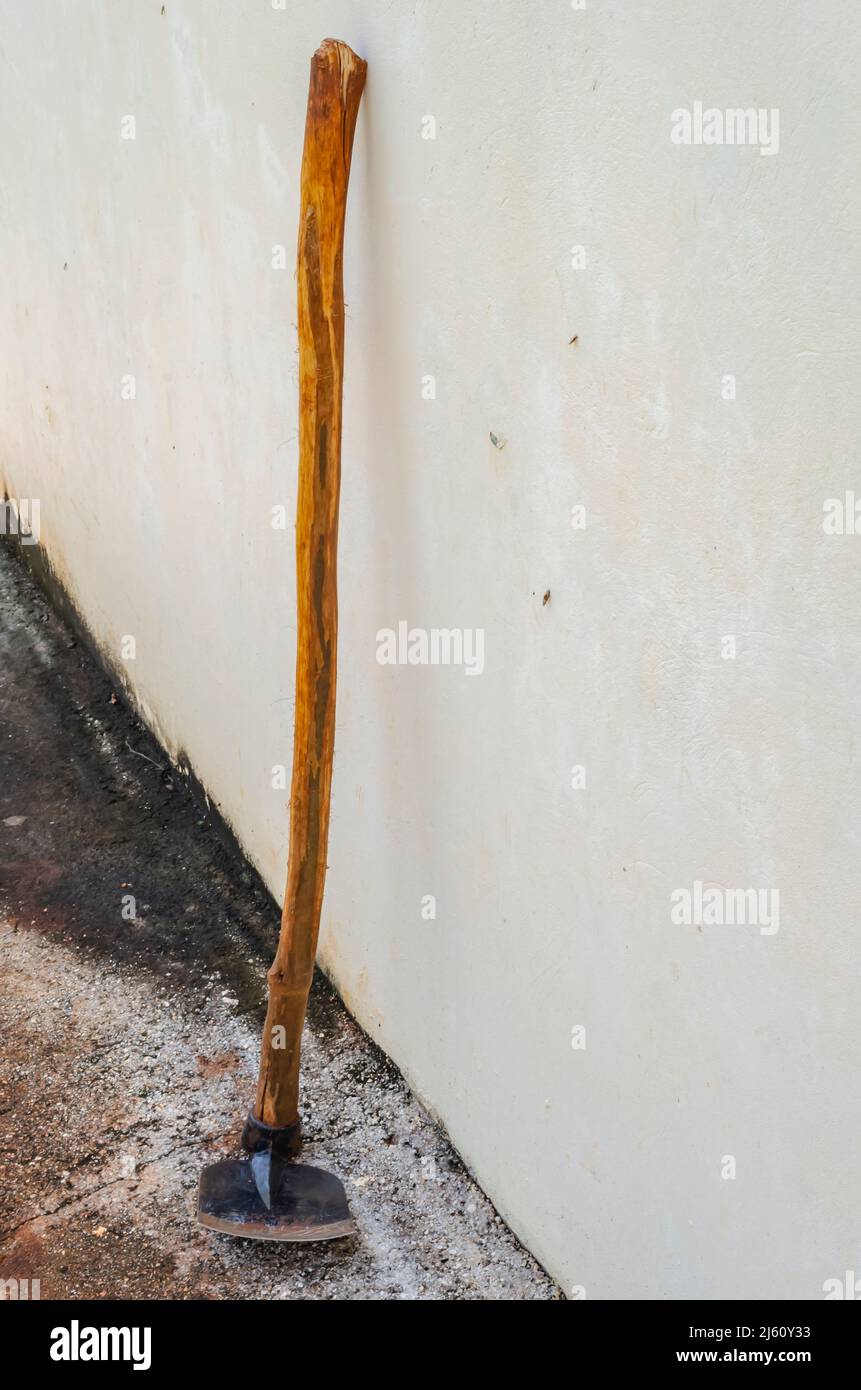 A black hoe with long wooden stick is leaning against a wall outside ...