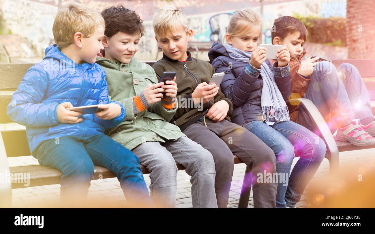 Kids playing with smartphones on bench Stock Photo - Alamy