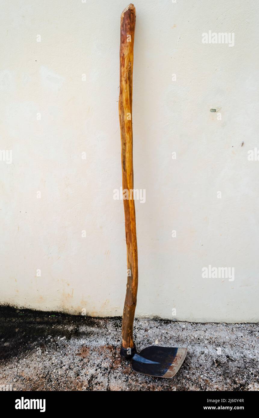 A black hoe with long wooden stick is leaning against a wall outside ...