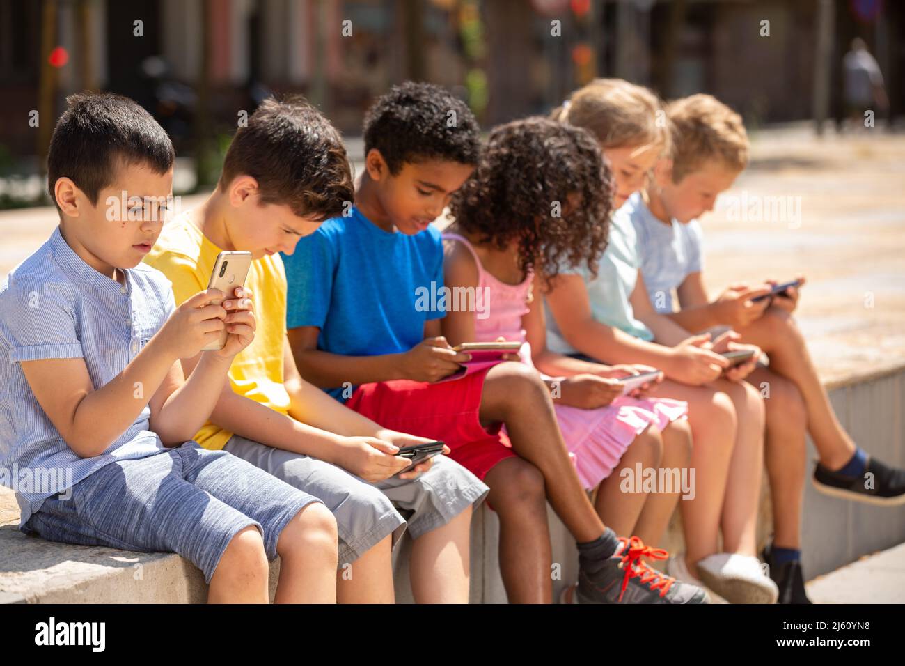 Positive children with mobile devices sitting at urban street Stock ...