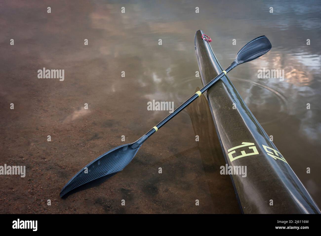 bow of narrow racing kayak with a wing paddle on a shore of calm lake ...