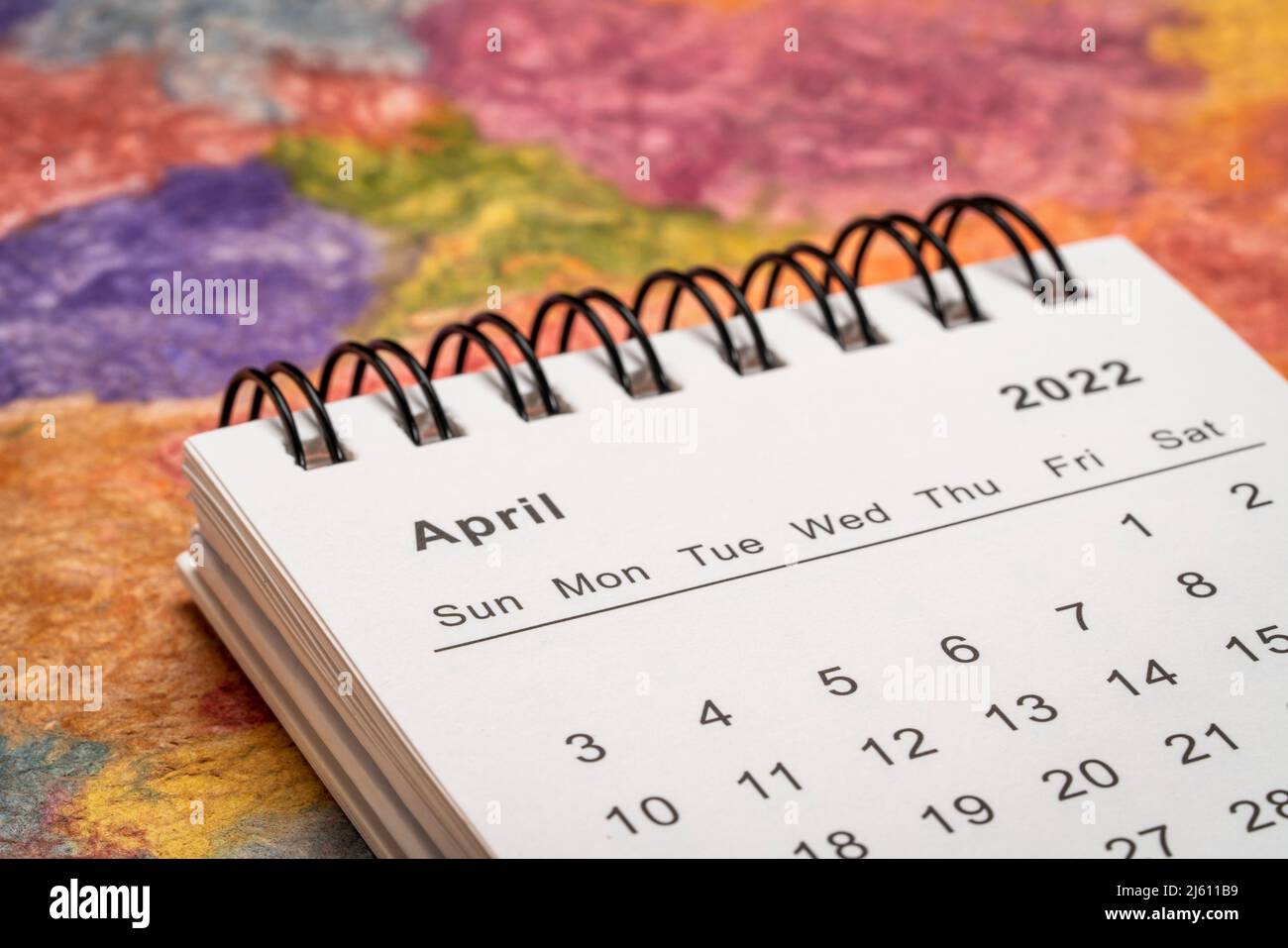 April 2022 - spiral desktop calendar against colorful handmade paper ...