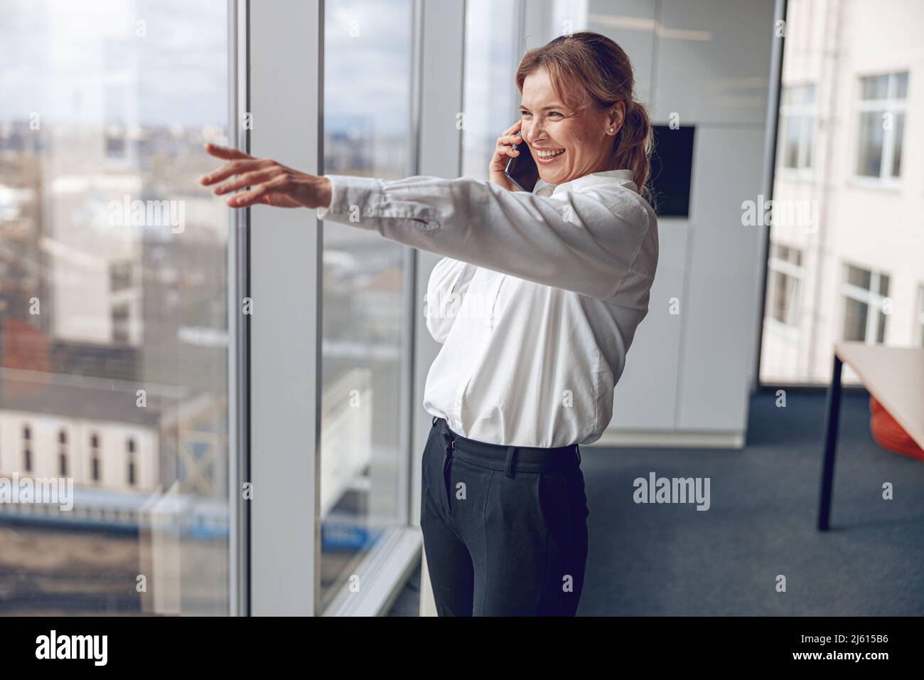 Businesswoman Making Phone Call Standing By Office Window and showing ...