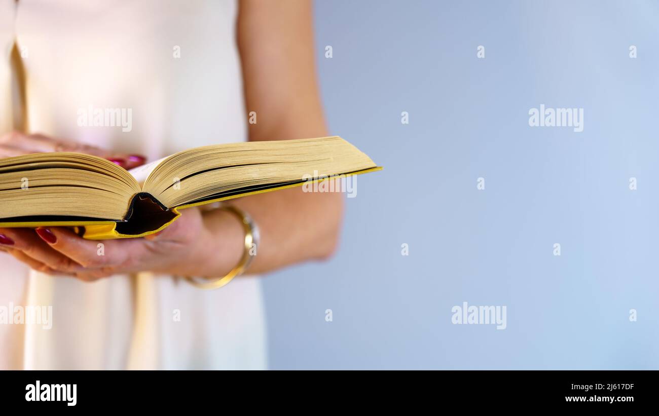 Woman holding a book and reading in standing posture on blue background ...
