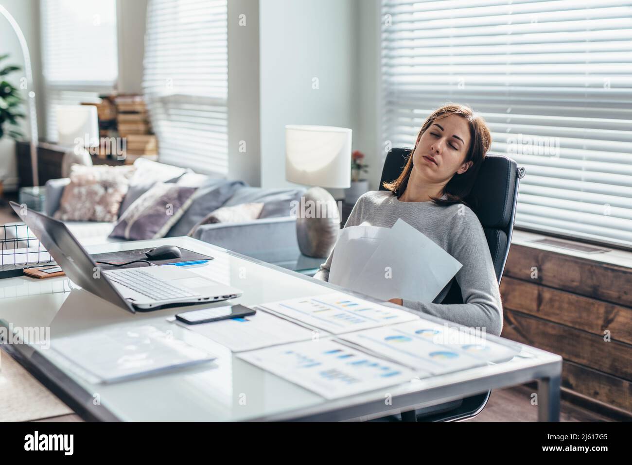 Woman at her desk asleep sitting on a chair holding paper to her chest ...