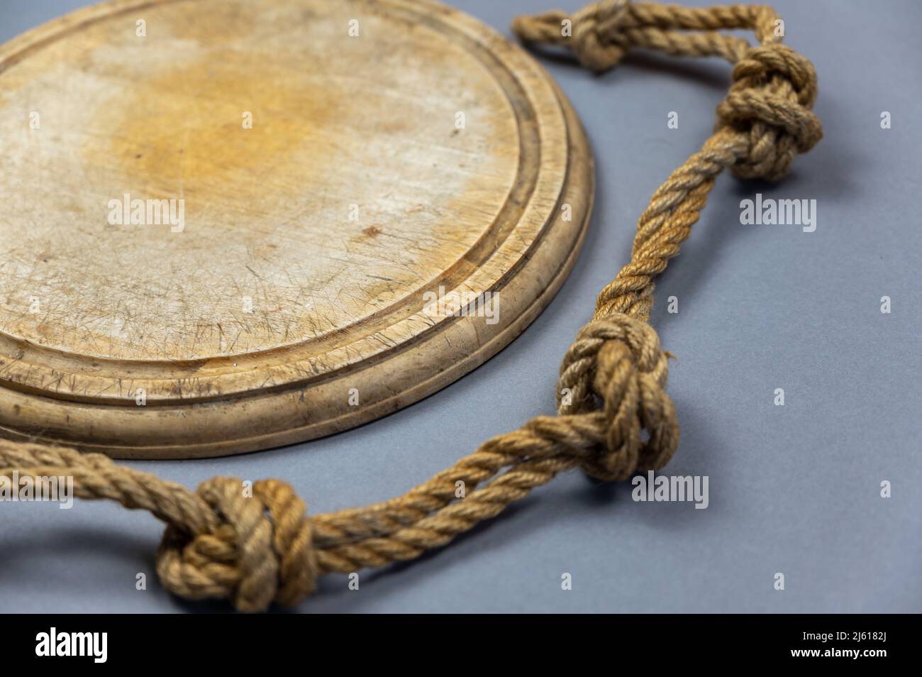Round wooden cutting board and ship's rope against the gray background ...