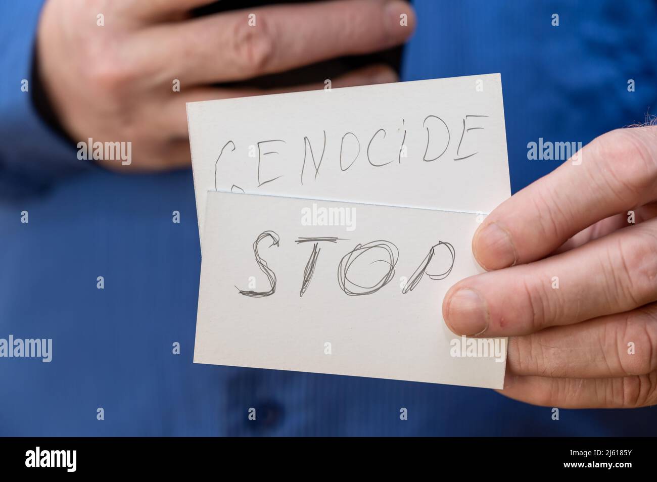 Stop Genocide. Inscription in jagged gray letters on paper. Man holding ...