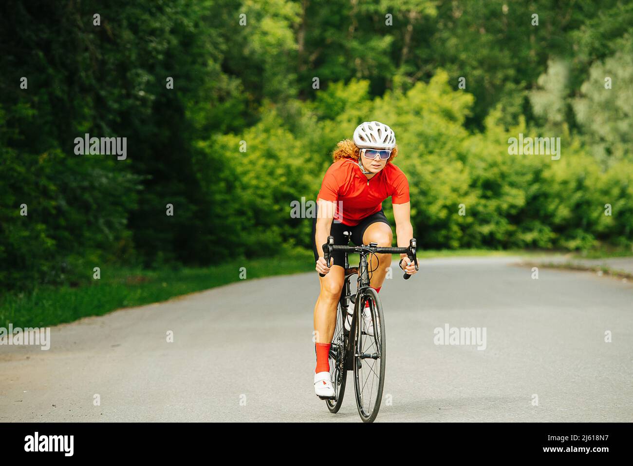 Fit woman riding her street racing bike on a road through the park ...