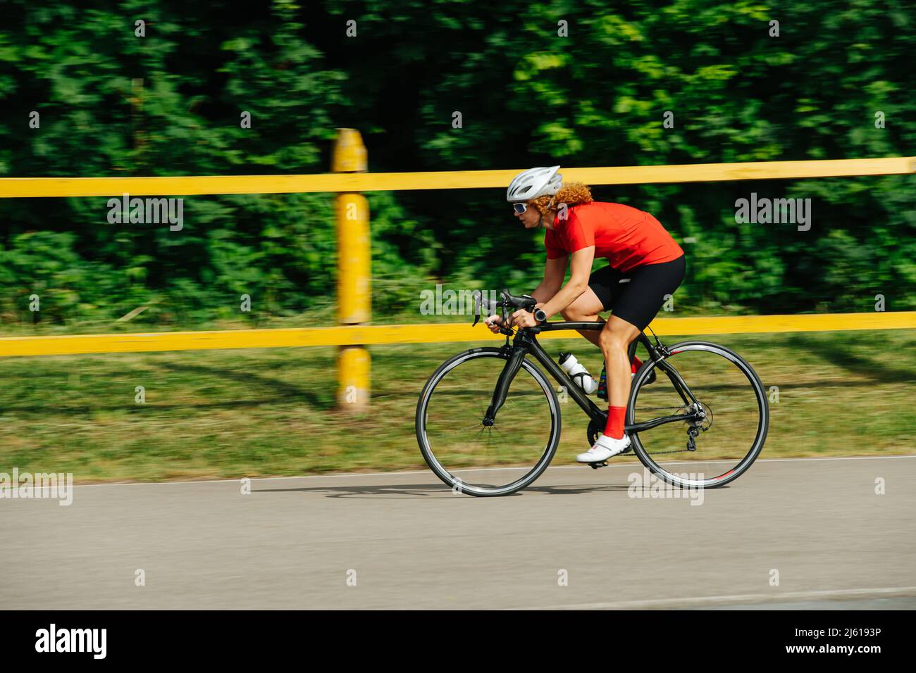 Redhead woman with curly hair in a helmet riding street racing bike on ...