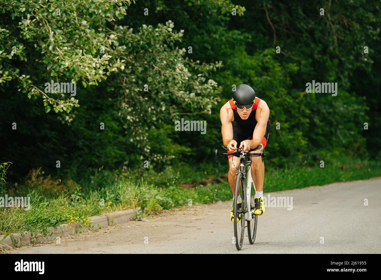 Muscular man riding his street racing bike on a road through the park ...