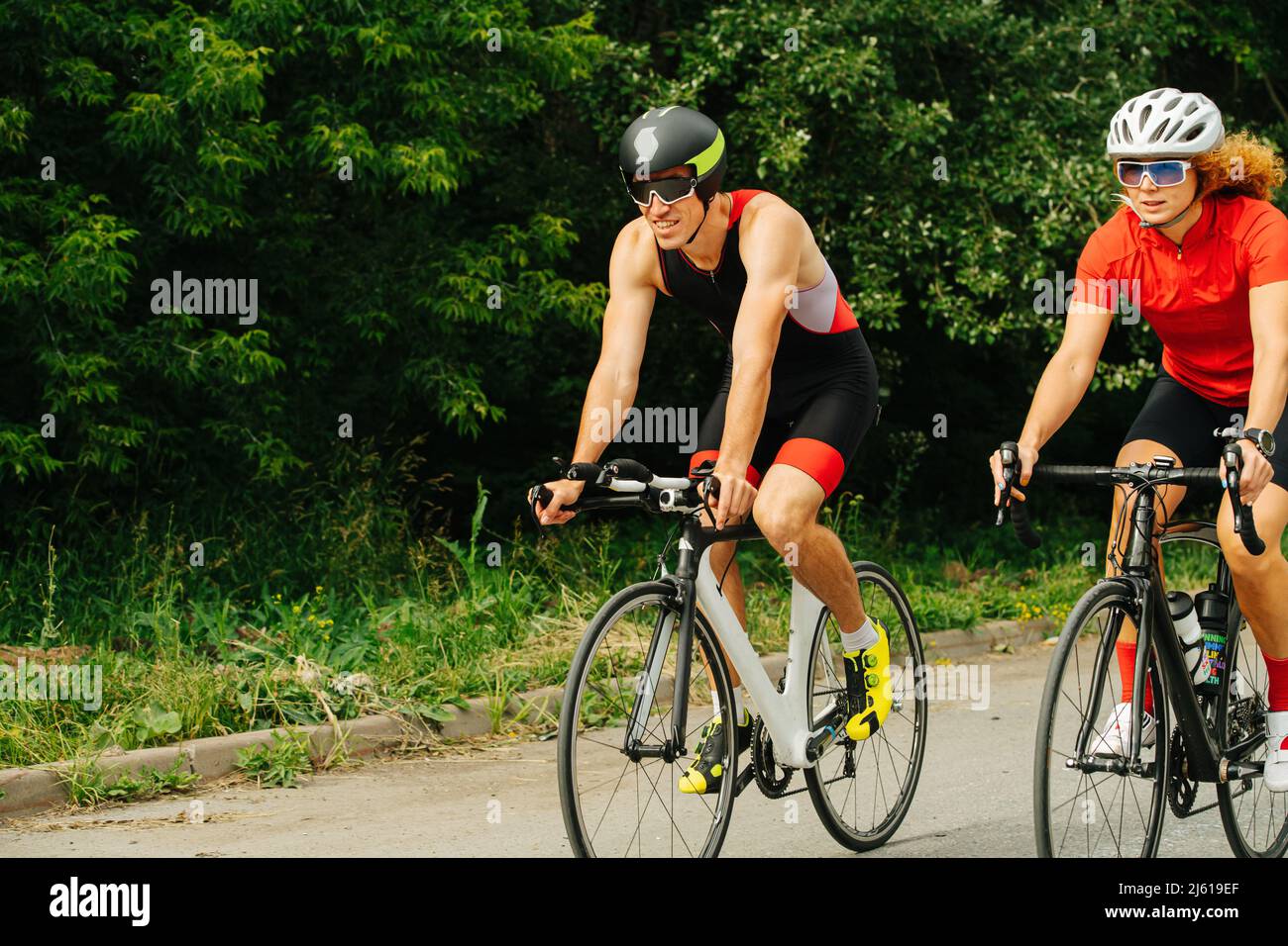 Athletic couple riding street racing bike on a road through the park ...
