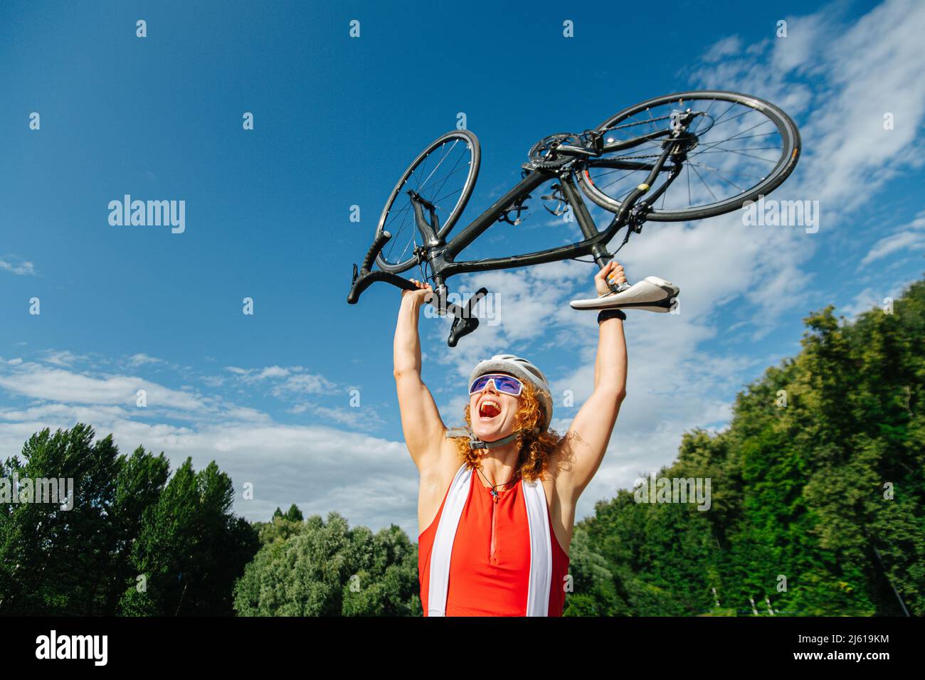Triumphant low angle picture of a woman cyclist lifting her bike over ...