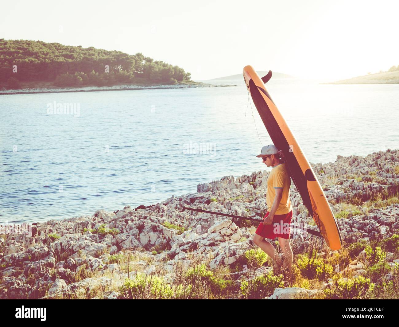 man walking down to beach with paddle board to go stand up paddeling ...