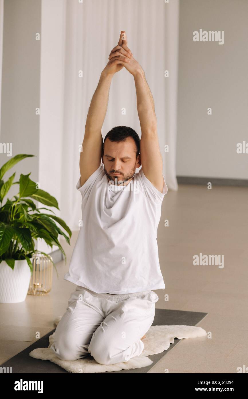 a man in white sportswear is doing yoga with a fitness room. the ...