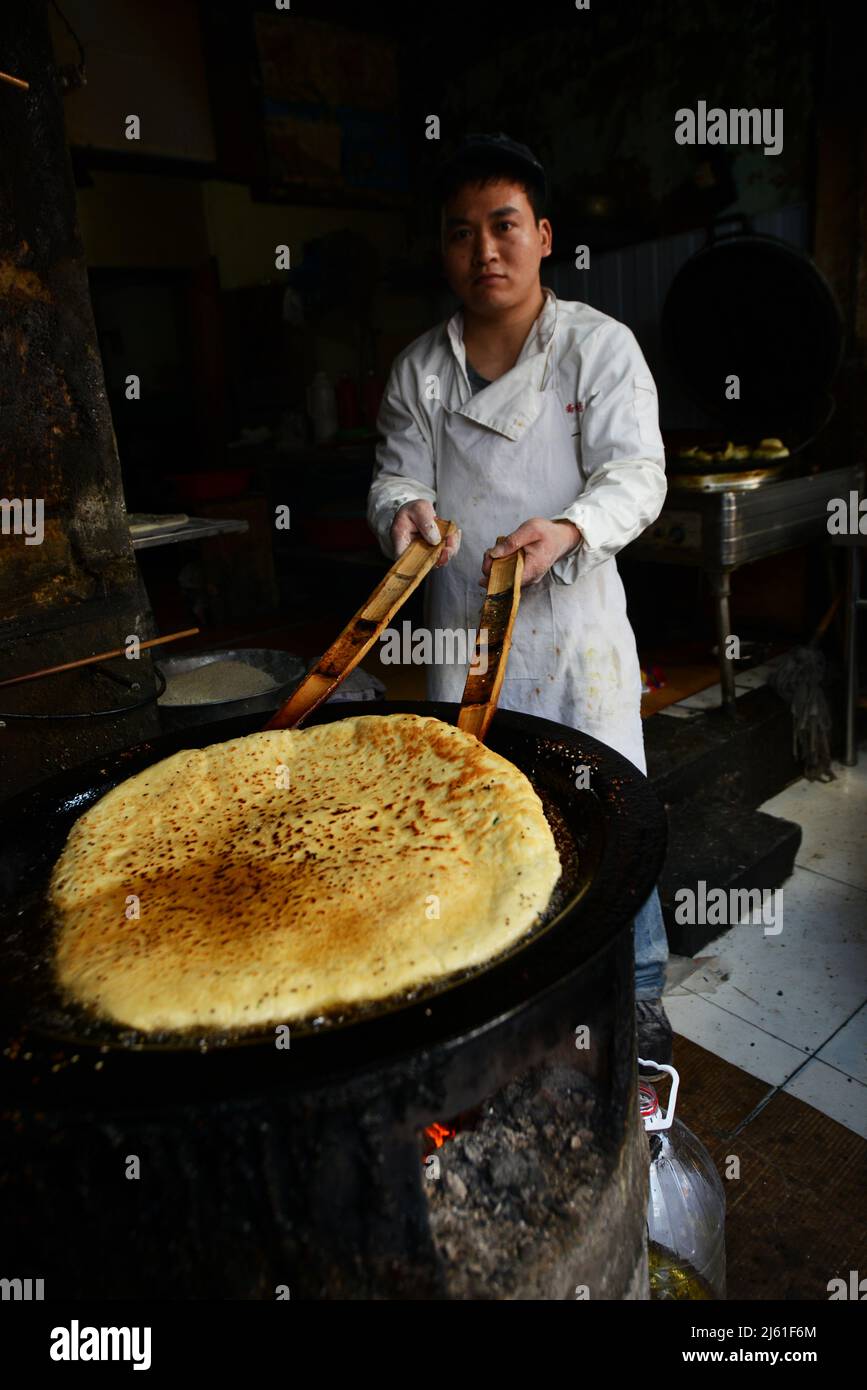A Chinese man frying a large traditional flat bread called Bing in a ...