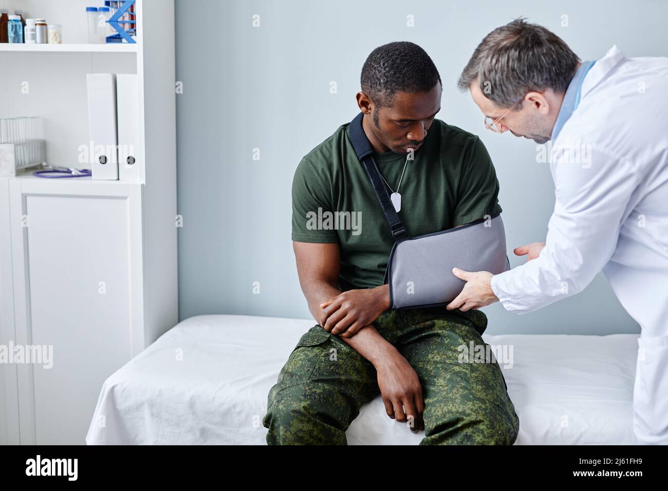 Mature Caucasian traumatologist palpating young African American ...
