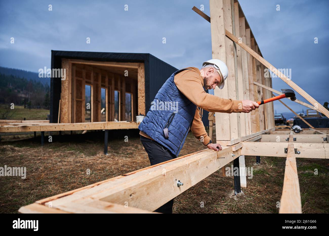 Man worker building wooden frame house on pile foundation. Carpenter ...