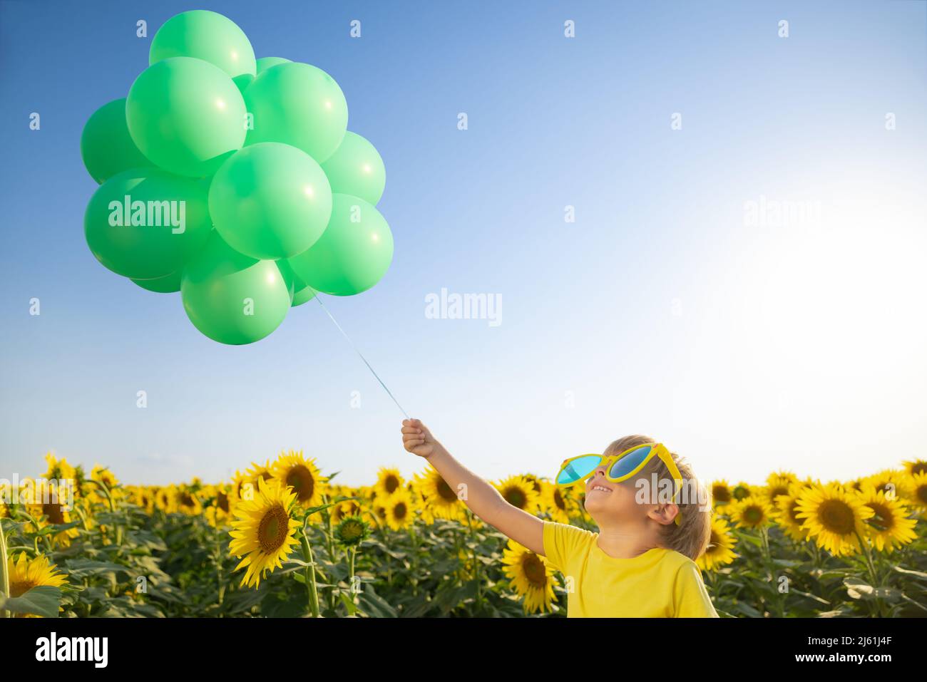Happy child having fun in spring field of sunflowers. Outdoor portrait ...