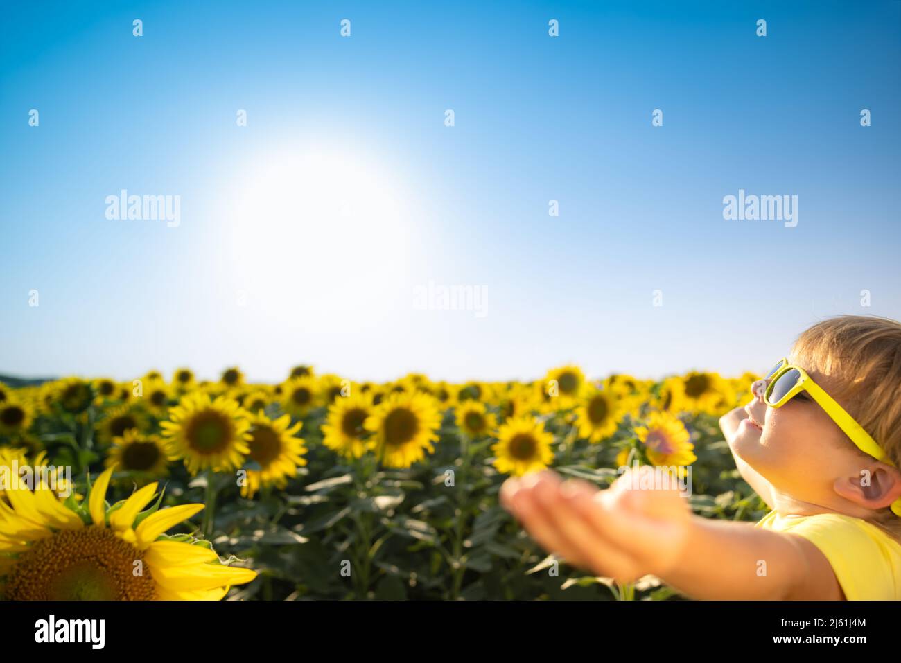 Happy child having fun in spring field of sunflowers. Outdoor portrait ...