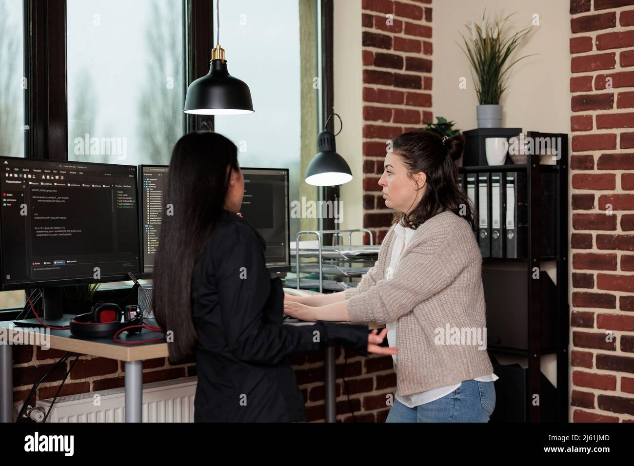 Company programmers standing near desk with multiple monitors on top of it. Network developers ...
