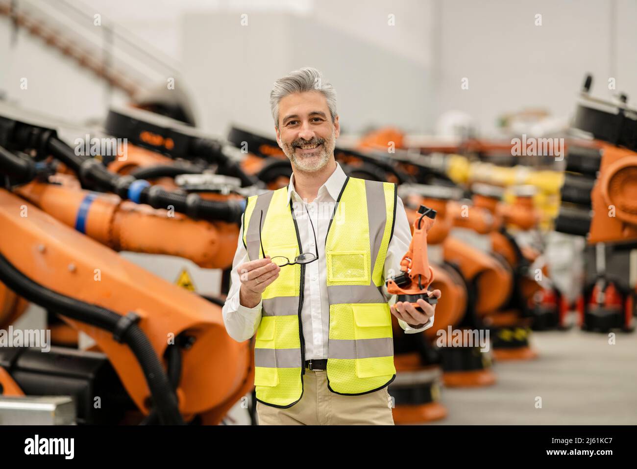 Smiling engineer holding model of robotic arm and eyeglasses standing ...