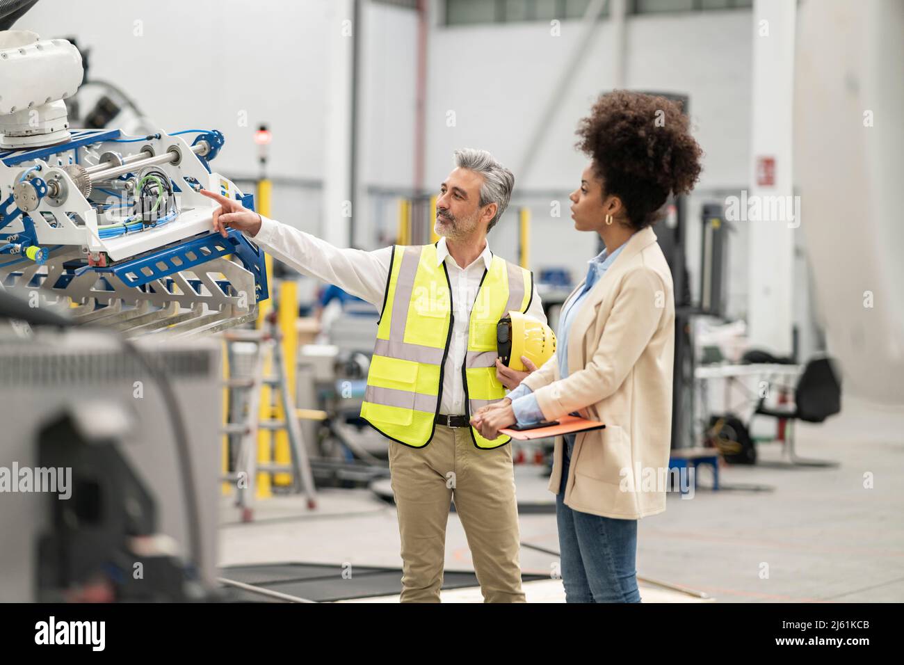 Engineer pointing at robotic arm discussing with businesswoman holding ...
