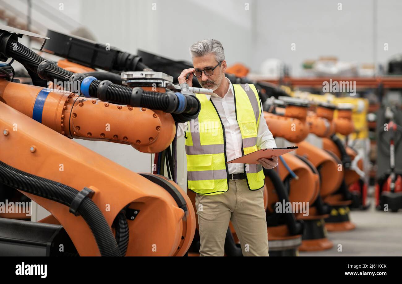 Engineer holding file folder analyzing robotic arms in factory Stock ...