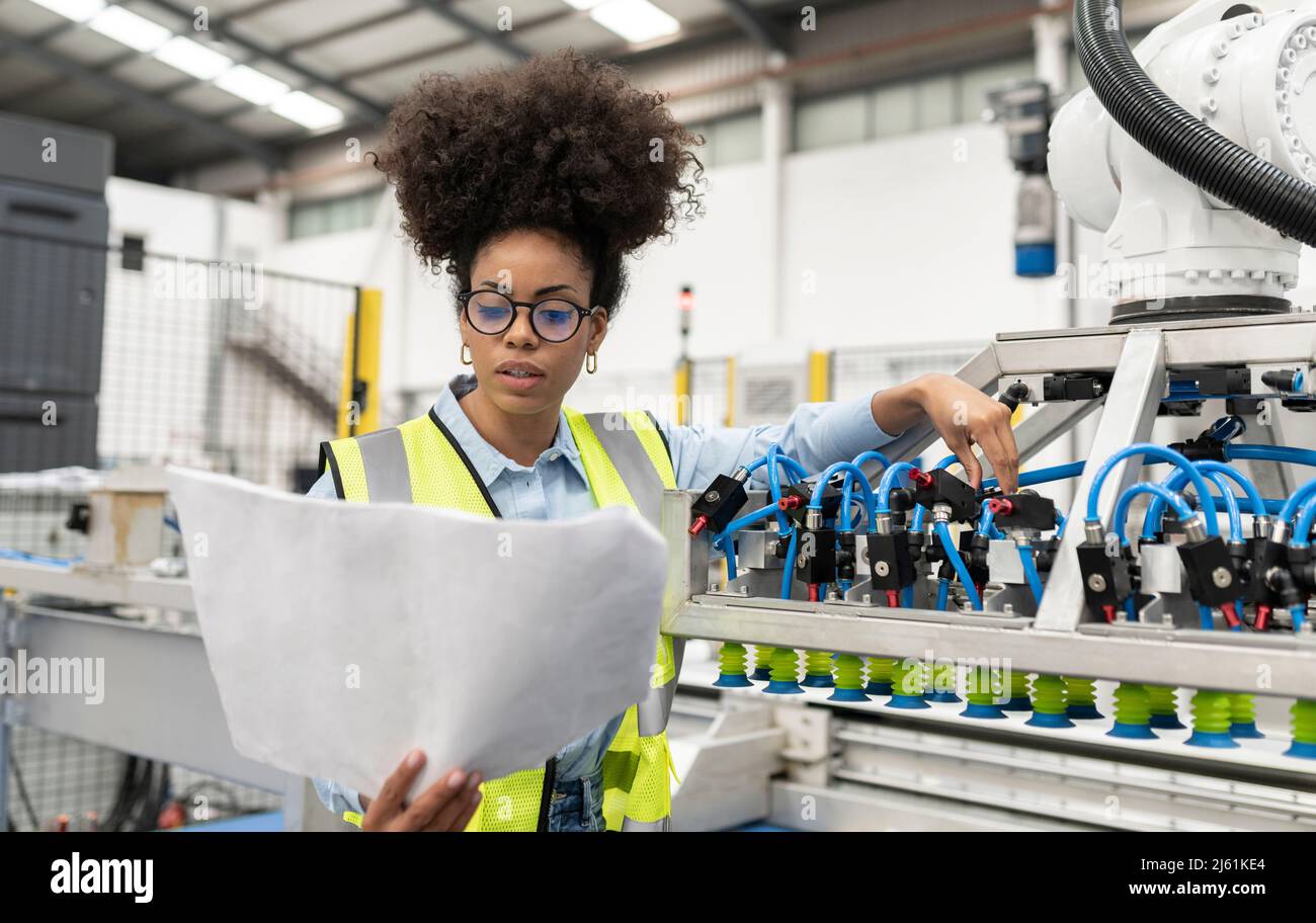 Engineer reading blueprint standing by robotic arm machine in factory ...