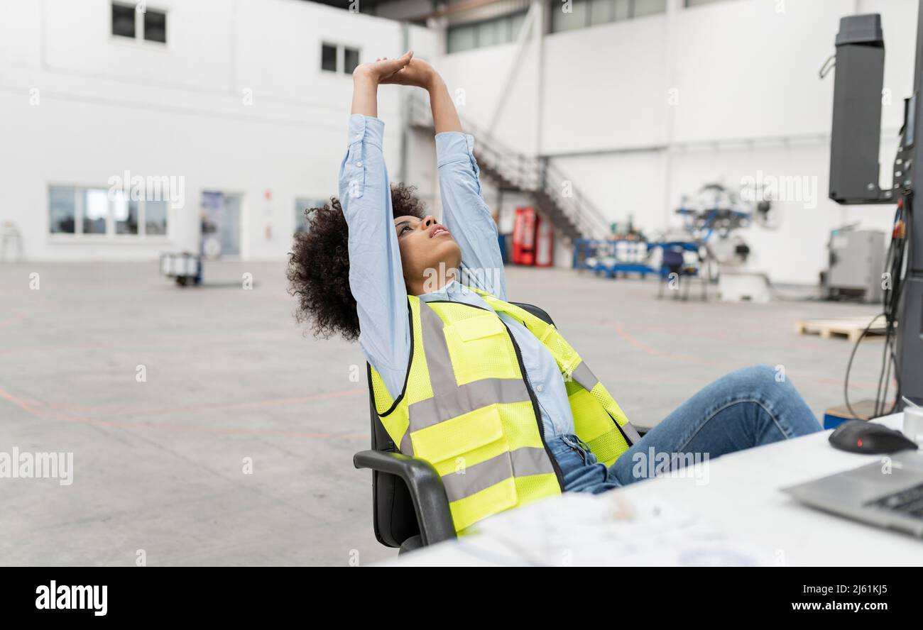 Engineer stretching hands sitting on chair in factory Stock Photo - Alamy