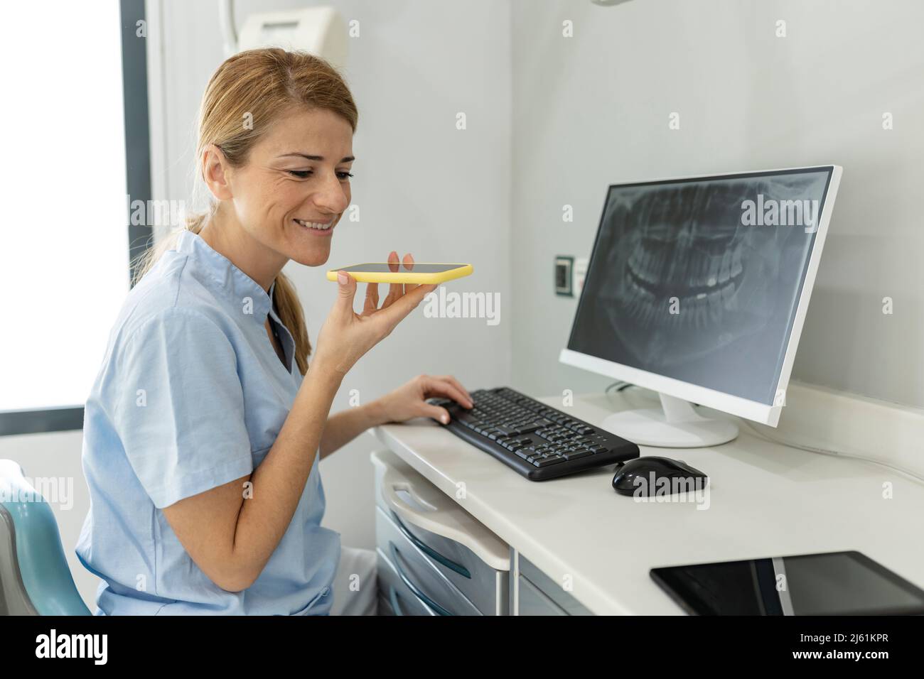 Smiling dentist talking on mobile phone through speaker at dental ...