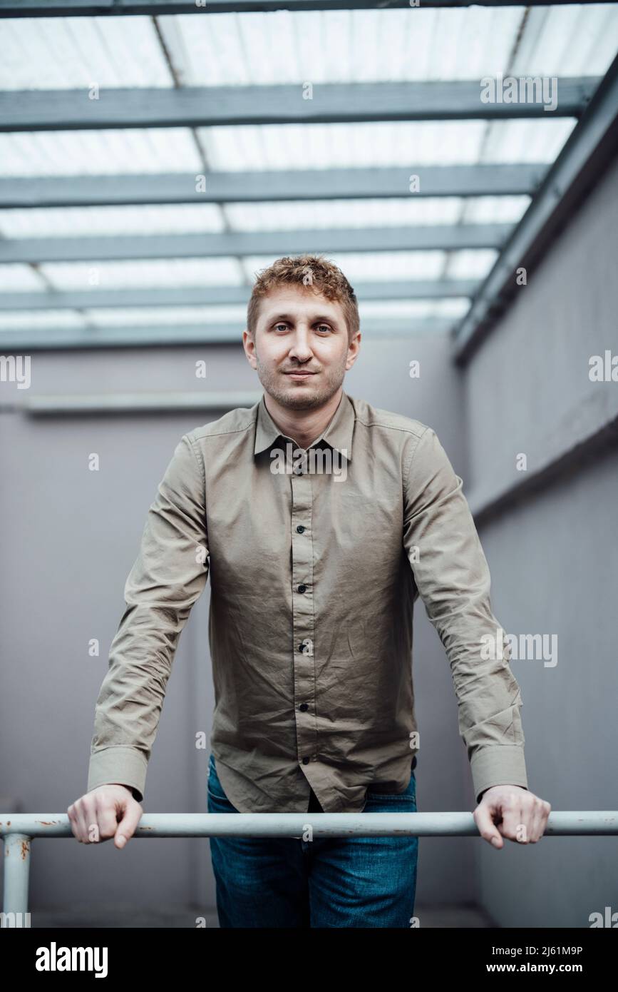 Businessman leaning on railing at work place Stock Photo - Alamy