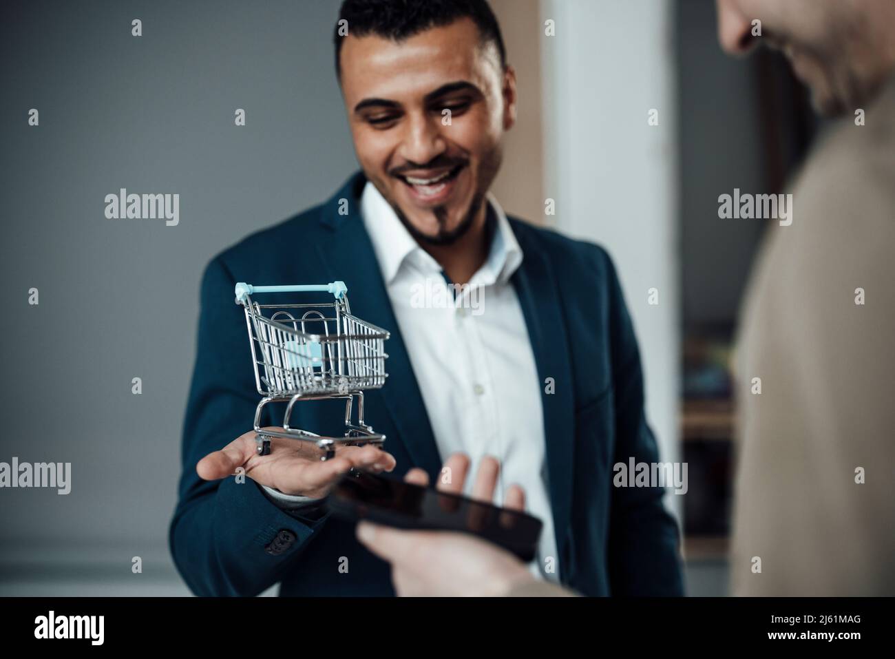 Happy businessman showing shopping cart model to colleague at office ...