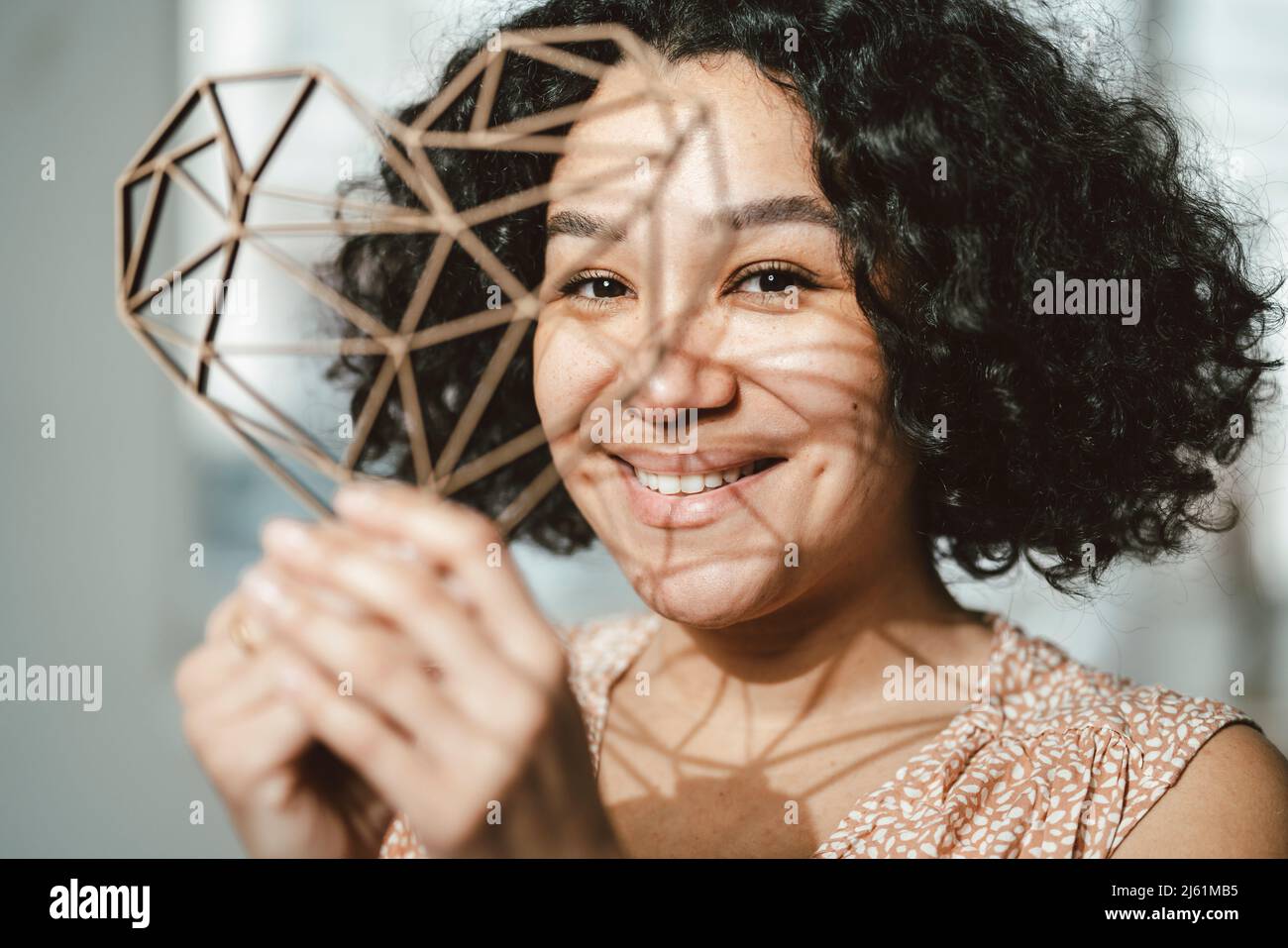Smiling woman with black curly hair holding heart shaped object Stock ...