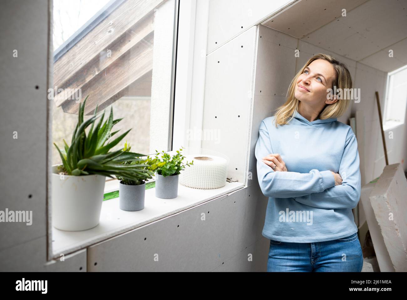 Smiling blond woman with arms crossed standing by window in attic Stock ...