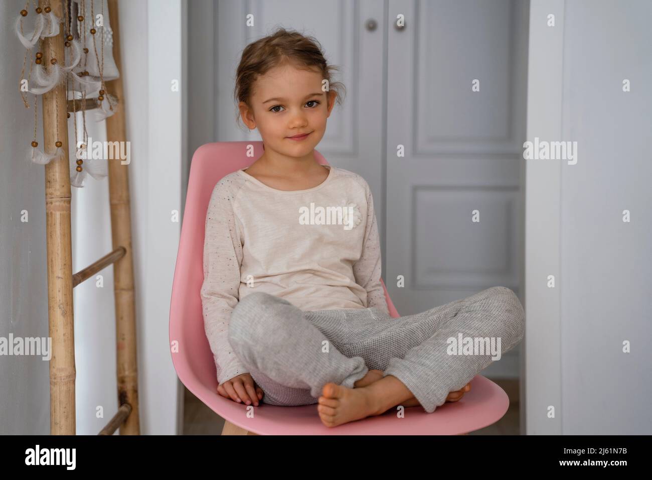 Cute girl sitting cross-legged on pink chair at home Stock Photo - Alamy