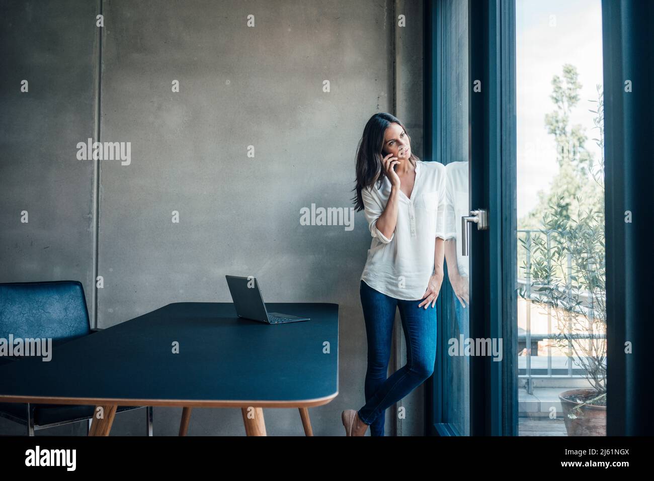 Woman talking on mobile phone looking through glass window at home ...