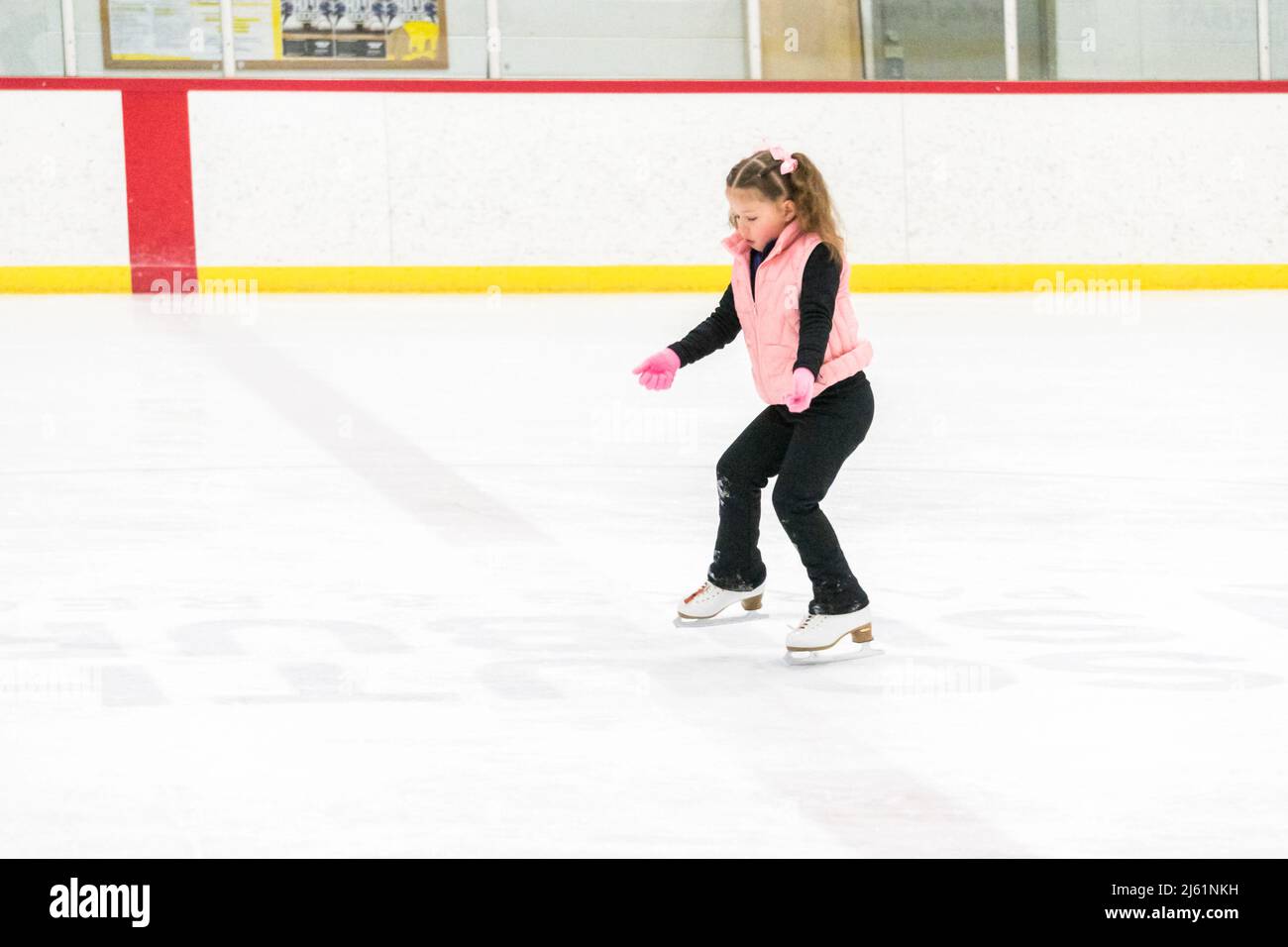Little girl practicing figure skating moves on the indoor ice rink ...