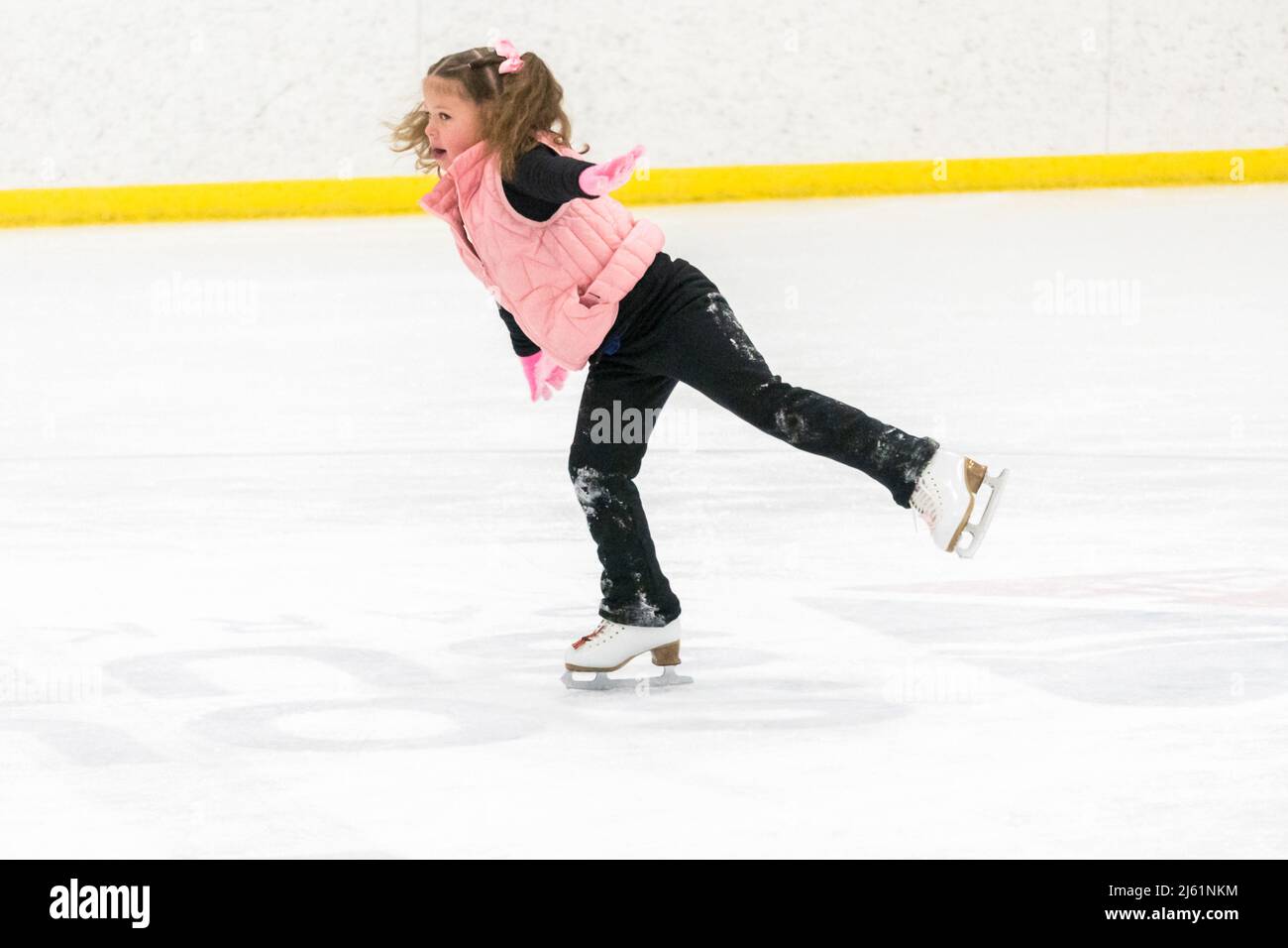 Little girl practicing figure skating moves on the indoor ice rink ...