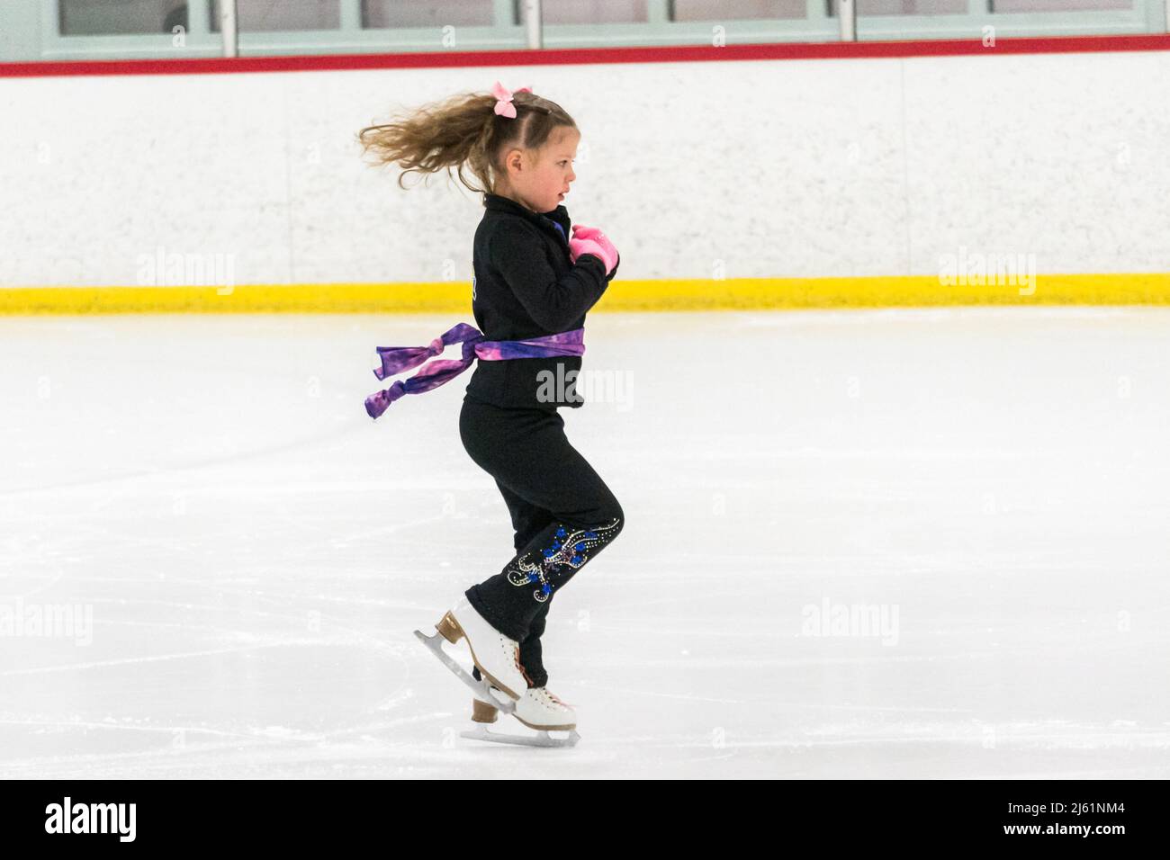 Little girl practicing figure skating moves on the indoor ice rink ...